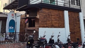 Um edifício moderno com estrutura em dois andares, uma varanda com guarda-corpo de vidro e uma placa indicando serviço de transporte.