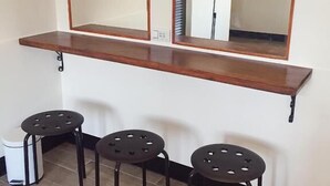Um canto com uma prateleira de madeira, um espelho e três banquetas pretas.