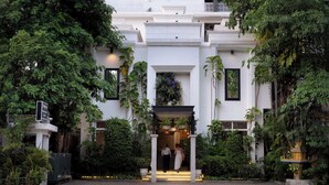Um edifício com fachada branca, rodeado por vegetação exuberante e uma entrada central com degraus.