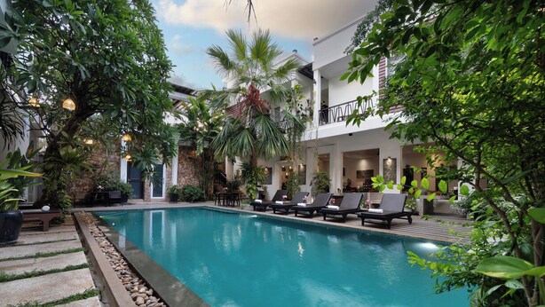 Área de piscina com espreguiçadeiras, parede de pedra e vegetação exuberante.