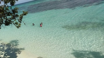 Uma praia com águas turquesa cristalinas e algumas pessoas nadando.