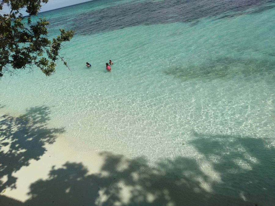 Uma praia com águas turquesa cristalinas e algumas pessoas nadando.