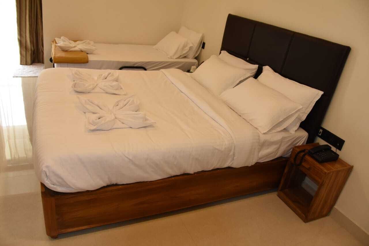 Quarto de hotel com uma cama grande, duas camas menores, cabeceira de madeira e mesa de cabeceira com telefone.