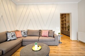 Uma sala de estar moderna com um sofá seccional, uma mesa de centro redonda com objetos decorativos e piso de madeira.