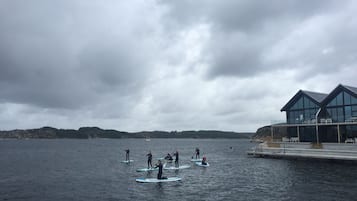 Um edifício à beira-mar com um cais e um grupo de pessoas praticando paddleboarding na água.