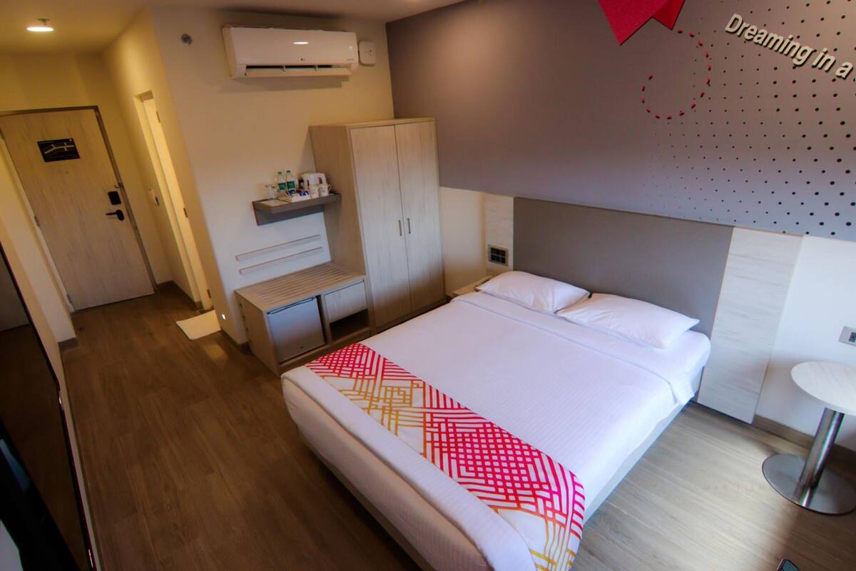 Quarto de hotel com cama, escrivaninha, guarda-roupa e uma mesinha.