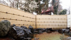 Uma onsen japonesa tradicional com cerca de bambu, terreno rochoso e piso de madeira.
