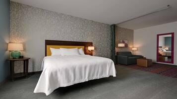 Quarto de hotel com uma cama grande, duas mesas de cabeceira com luminárias, um sofá e um espelho.