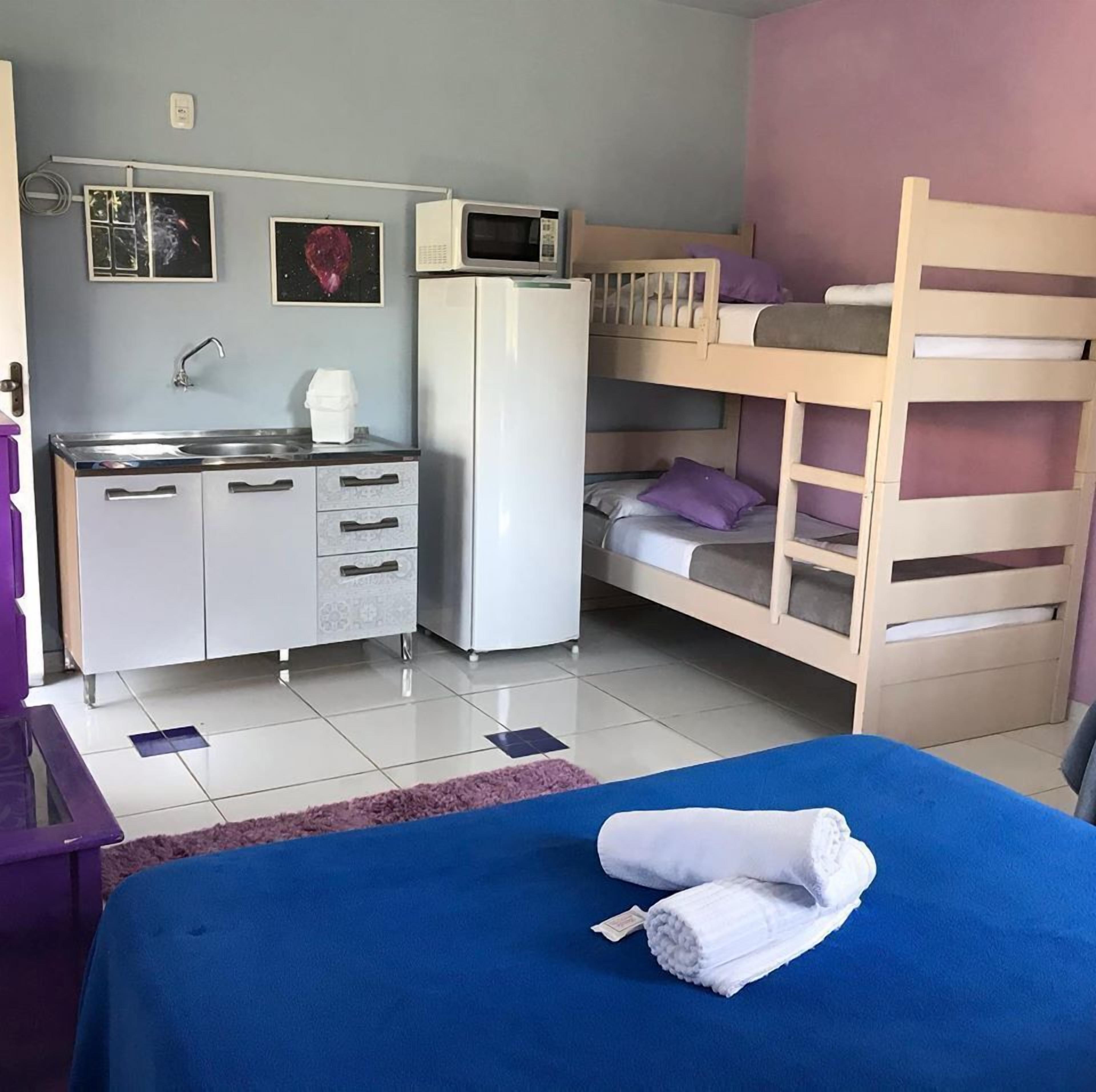 Quarto compacto com beliche, cozinha compacta com geladeira e cama com cobertura azul.