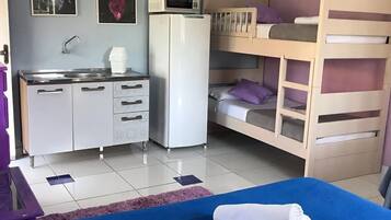 Quarto compacto com beliche, cozinha compacta com geladeira e cama com cobertura azul.