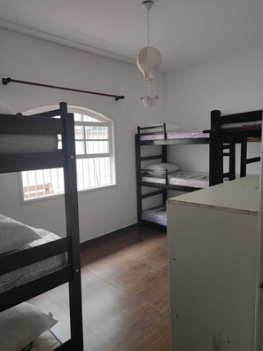 Um dormitório com beliches, uma janela com grades, um lustre e um armário branco.