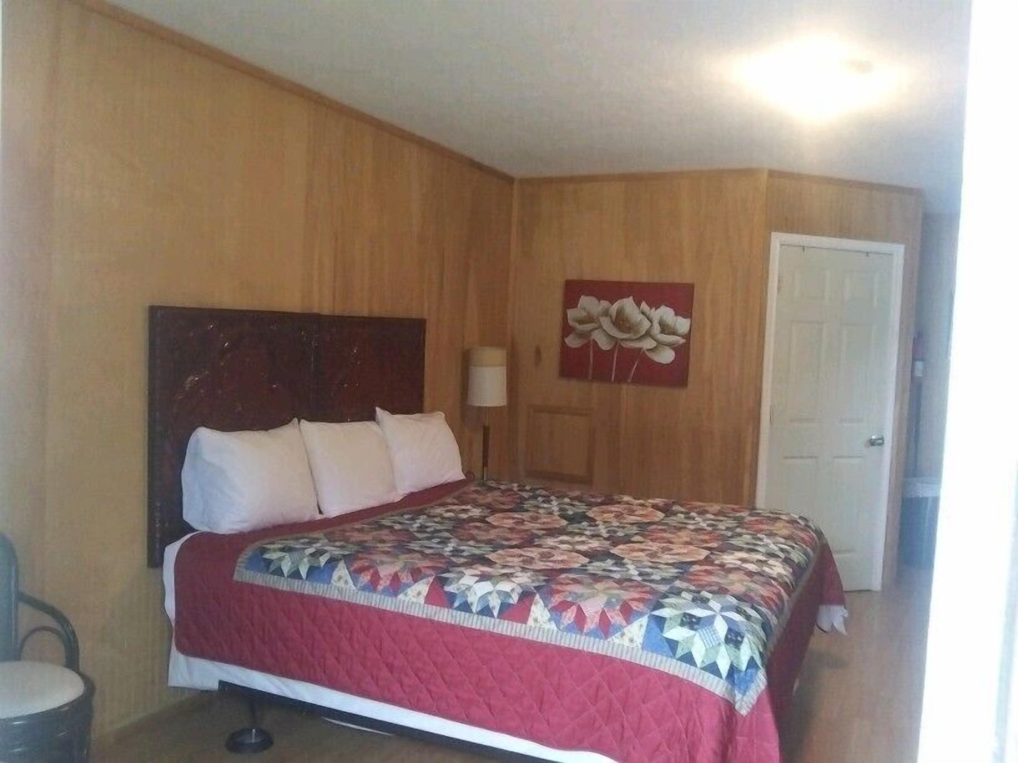 Quarto com cabeceira de madeira, colcha acolchoada, luminária na parede e uma porta.