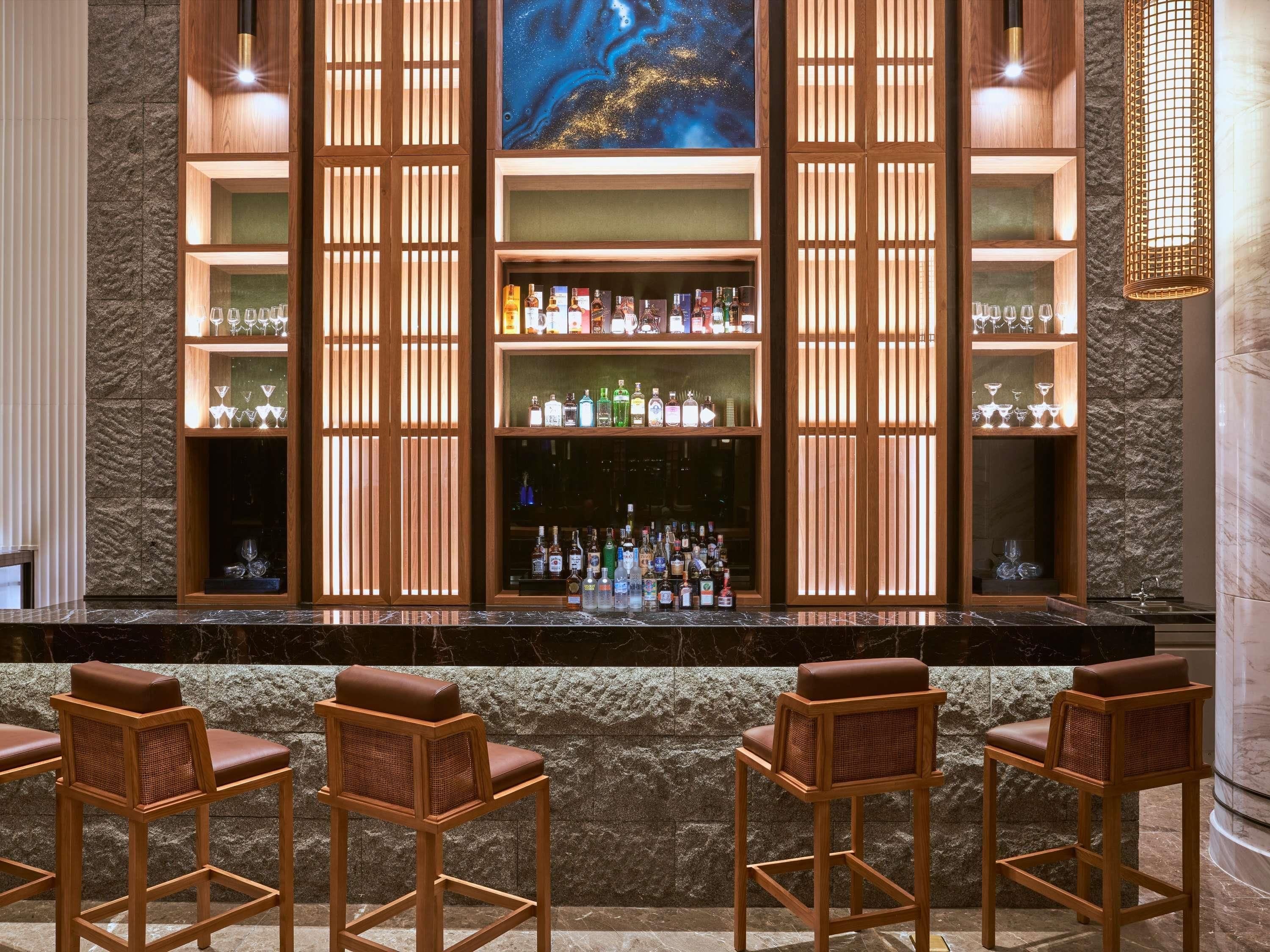 Uma área de bar com prateleiras de madeira, banquetas e uma grande pintura na parede.