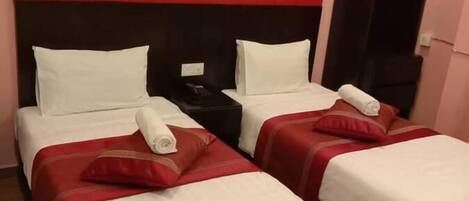 Quarto de hotel com duas camas, cada uma com roupa de cama branca e detalhes vermelhos. Possui cabeceira preta e uma parede com detalhes vermelhos.