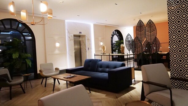Um hall moderno com um sofá azul, cadeiras brancas, uma mesa de centro de madeira e uma parede estampada.