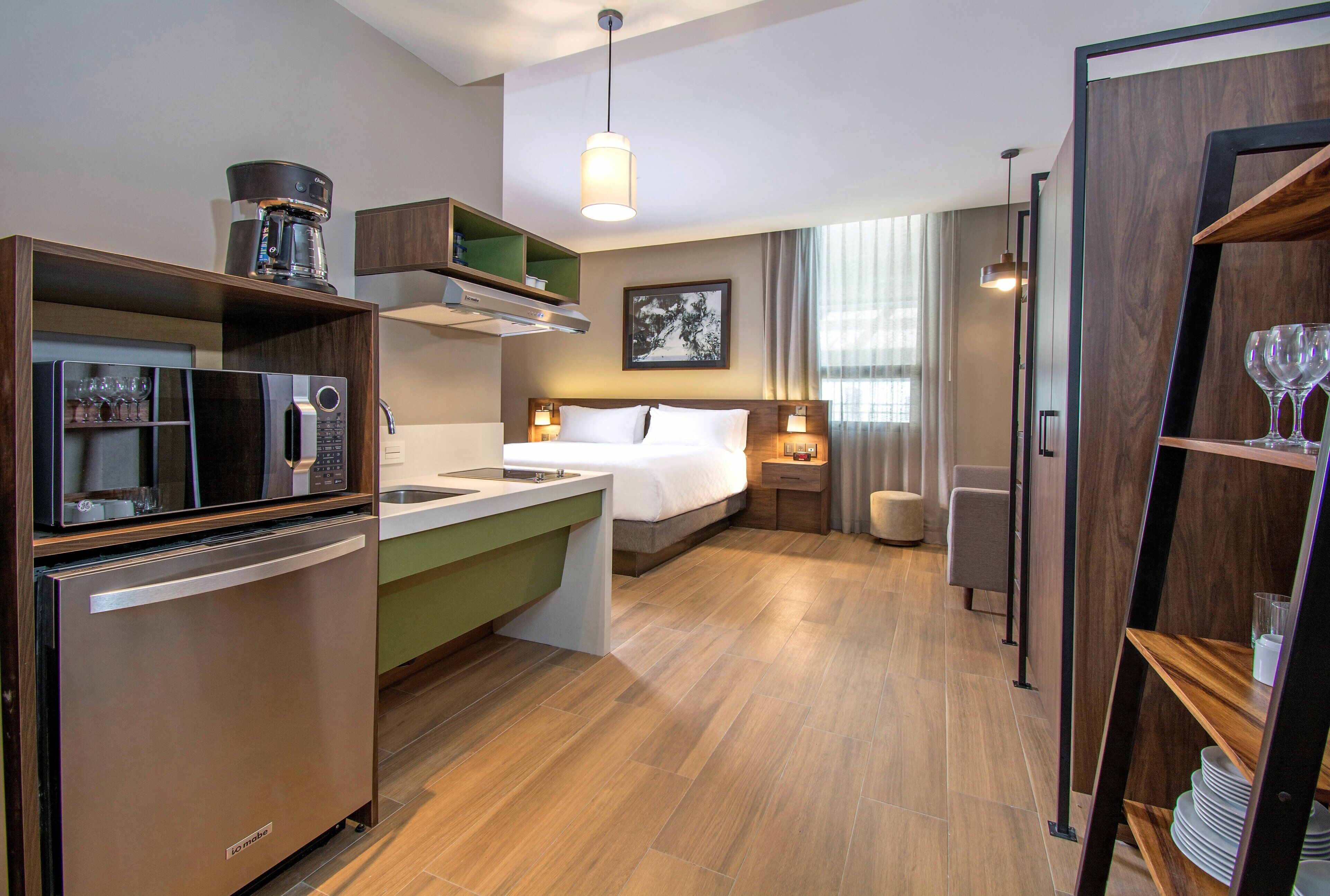Quarto de hotel moderno com cozinha compacta, cama, área de estar e vista para o exterior.