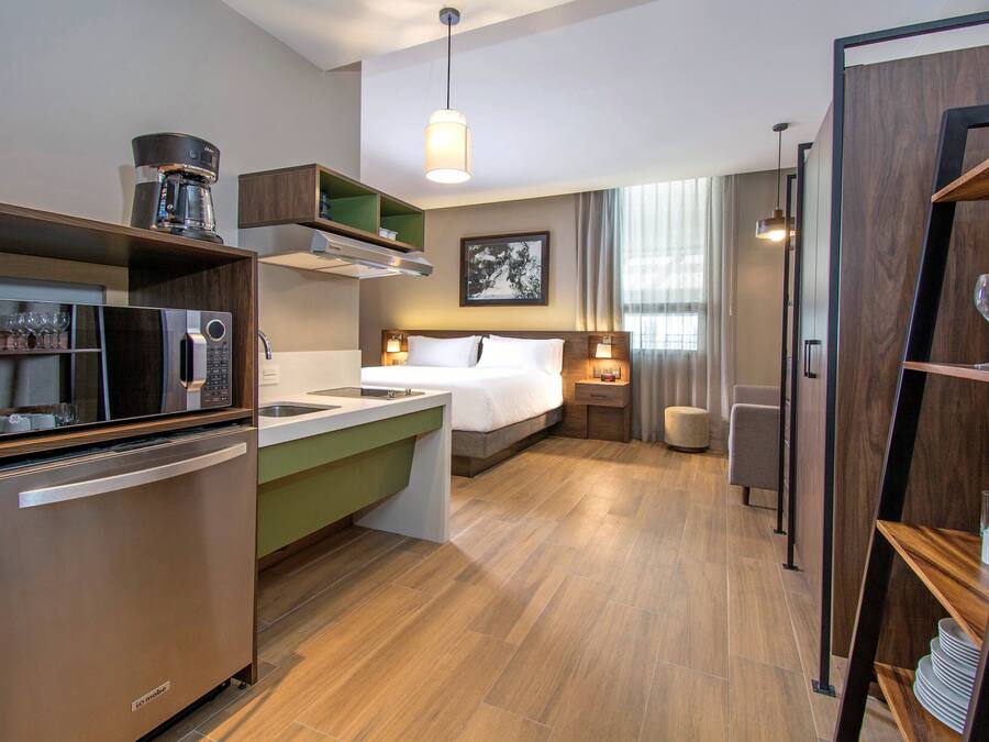 Quarto de hotel moderno com cozinha compacta, cama, área de estar e vista para o exterior.