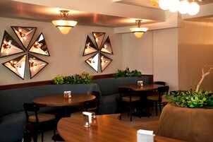 Um restaurante com mesas redondas e cabines, espelhos decorativos na parede e luminárias pendentes.
