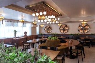 Interior moderno de restaurante com mesas redondas, assentos acolchoados e arte decorativa nas paredes.