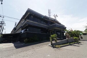 Um edifício de vários andares com um letreiro grande que diz 'HOTEL', apresentando um design arquitetônico moderno com sacadas e uma área frontal ajardinada.