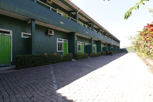 Um edifício com fachada verde, várias janelas e um calçadão pavimentado.