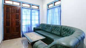 Um quarto com sofá de couro verde, porta de madeira e cortinas azuis.