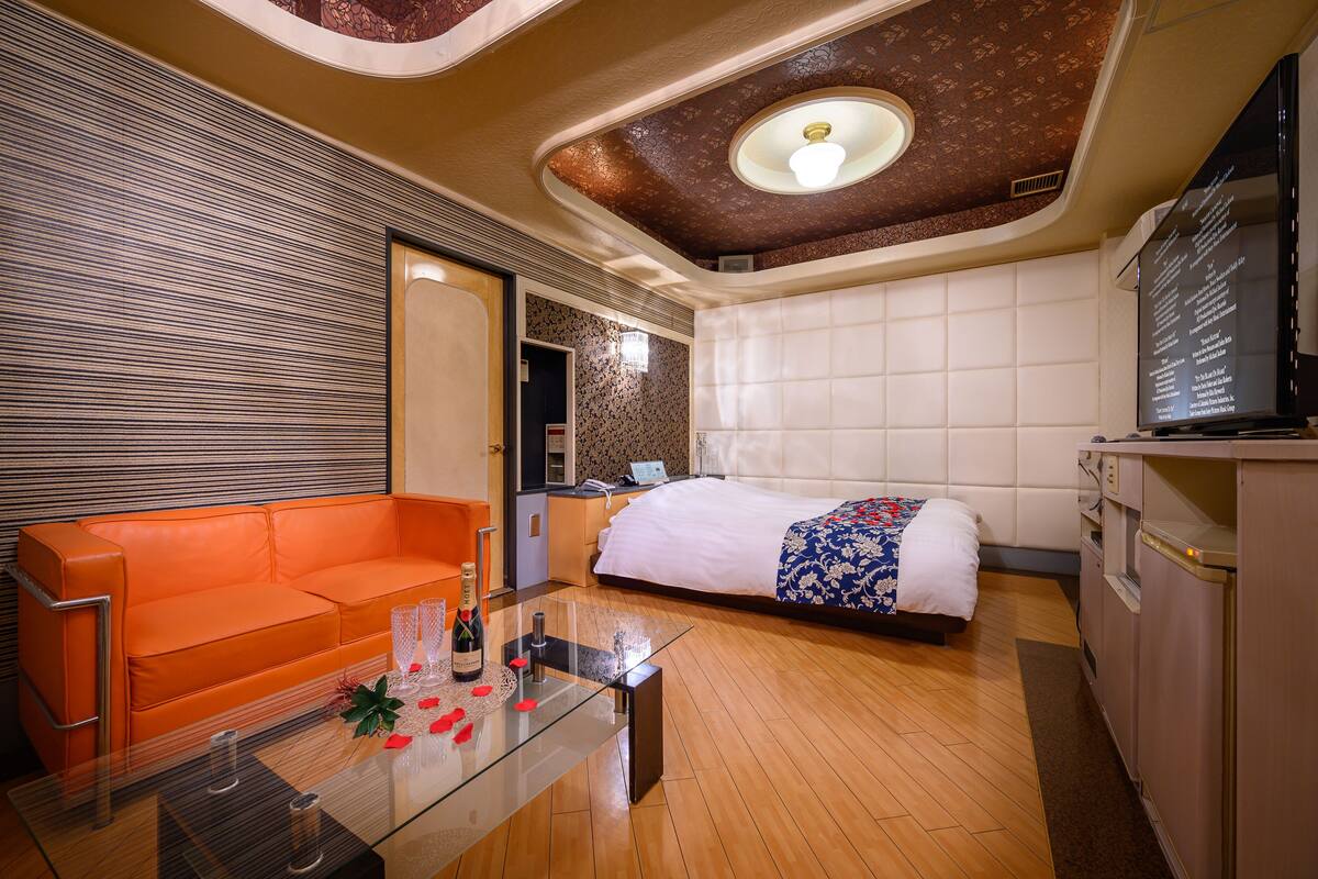 Quarto de hotel com cama, sofá, mesa de centro de vidro e televisão.