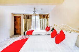Quarto de hotel com cama, ventoinha no teto, janela com cortinas e porta.