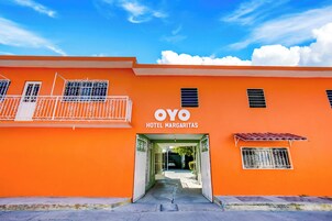 Um edifício com fachada laranja vibrante, uma placa indicando 'OYO HOTEL MARGARITAS' e uma entrada com portão.