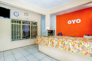 Uma área de recepção com uma mesa estampada com frutas coloridas, um relógio e uma parede com a marca OYO.