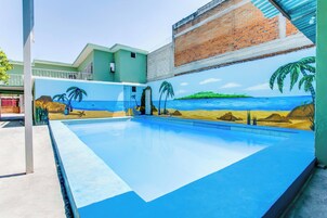 Uma piscina com um mural representando uma praia, incluindo palmeiras e um pôr do sol sobre o oceano.