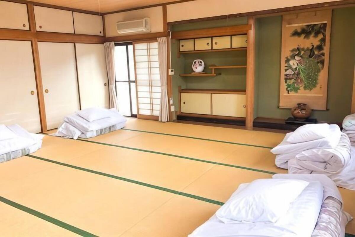 Um quarto com esteiras de tatame, futons, uma porta deslizante e uma prateleira com um relógio.
