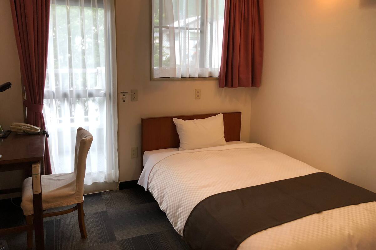 Quarto de hotel com uma cama, uma escrivaninha com telefone e uma cadeira.