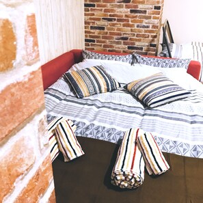 Uma cama com roupa de cama listrada, uma parede de tijolos e uma cadeira.