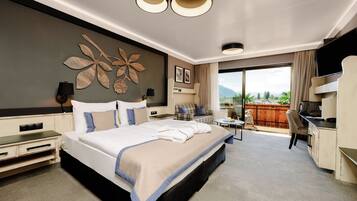 Quarto de hotel moderno com uma cama grande, uma escrivaninha, uma cadeira, uma televisão e uma varanda com vista.