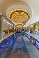 Uma área de piscina interior moderna com um elemento central de água, áreas de estar e um balcão de recepção.