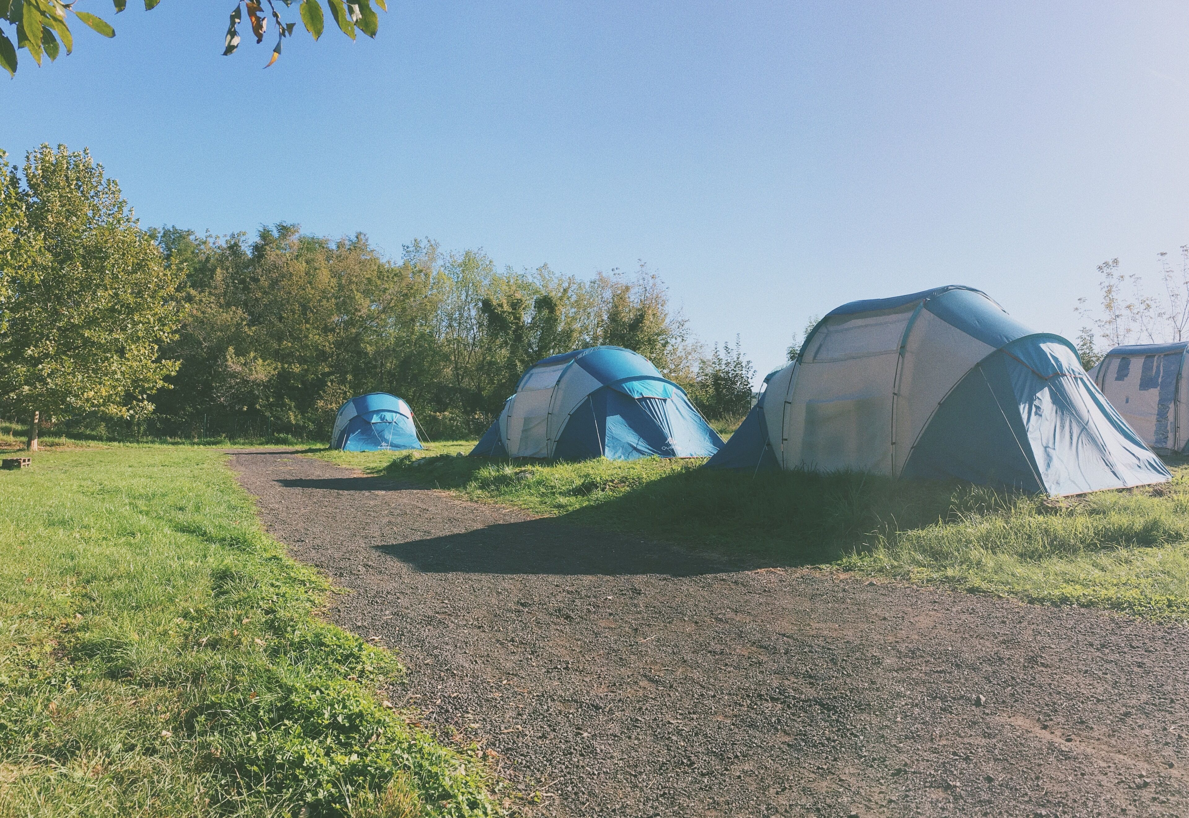 Um camping com várias tendas dispostas em fila ao longo de um caminho de cascalho.