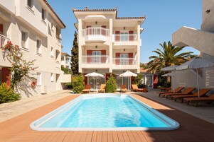 Piscina com espreguiçadeiras e guarda-sóis, cercada por um edifício com varandas e céu claro.