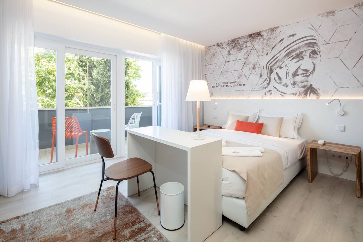 Quarto de hotel moderno com cama, escrivaninha, cadeira e vista para o exterior.