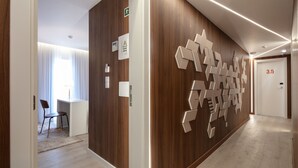 Um corredor moderno de hotel com lambris de madeira, uma instalação artística de arte geométrica e uma porta com a inscrição 3.5.