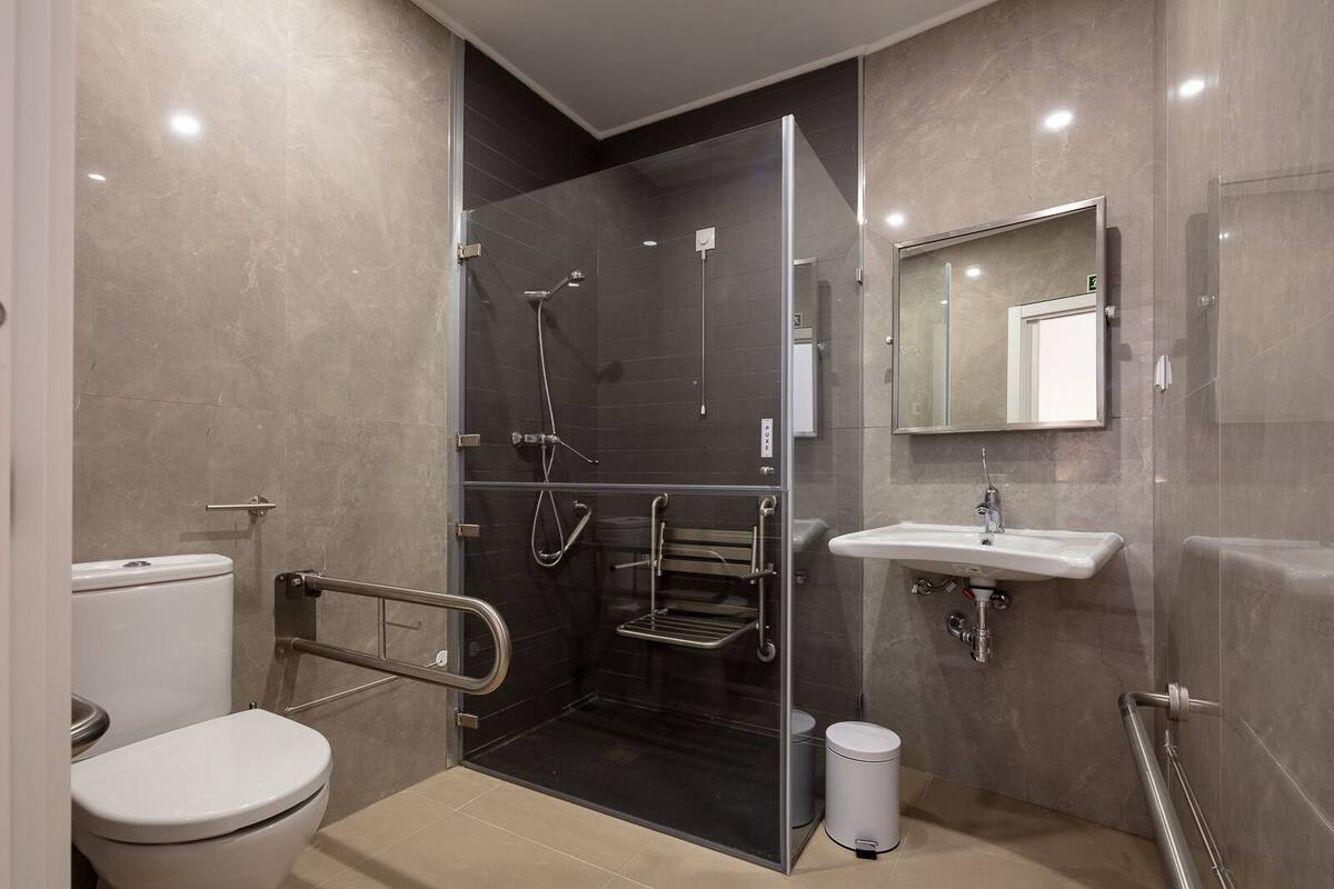 Uma casa de banho moderna com cabine de chuveiro em vidro, uma pia branca e uma sanita.