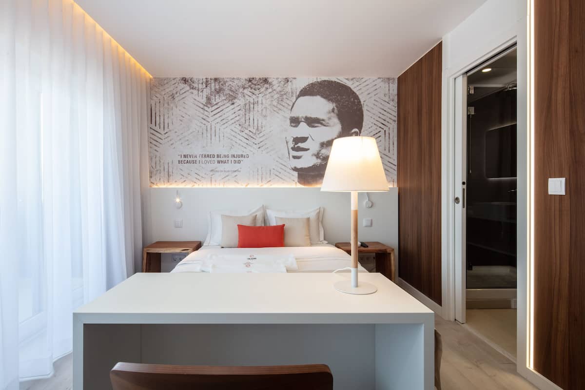 Quarto de hotel moderno com uma cama grande, mesa de cabeceira, abajur e guarda-roupa.