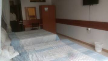 Quarto de hotel com duas camas, uma escrivaninha, uma cadeira, um guarda-roupa e uma televisão na parede.