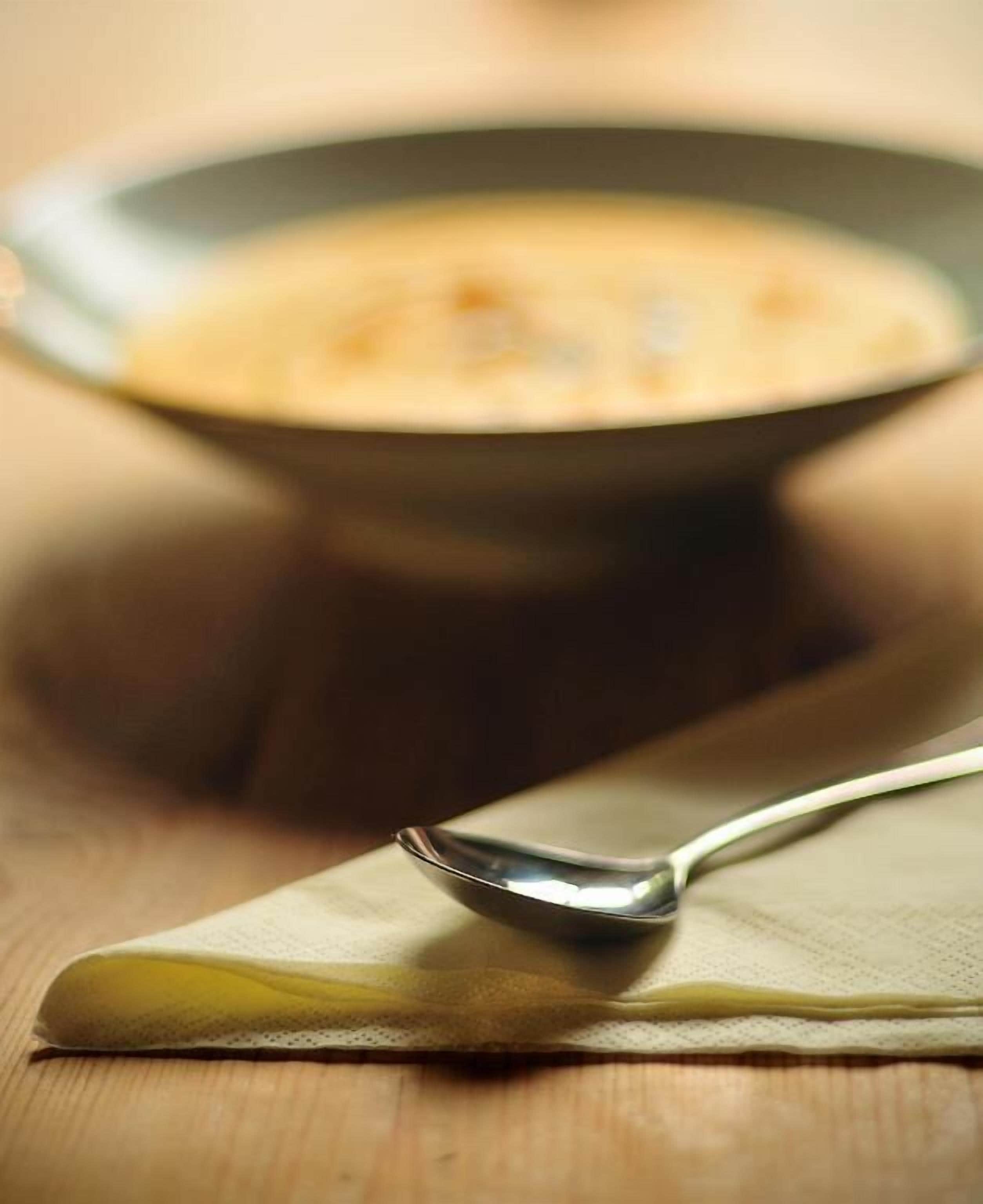 Uma tigela de sopa sobre uma mesa de madeira, com uma colher apoiada num guardanapo.