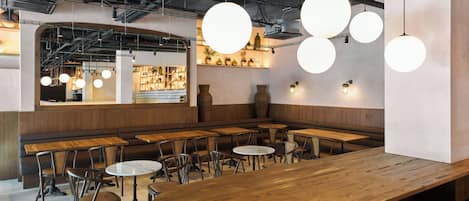 Interior de restaurante com mesas redondas, áreas de assento em cabines, luminárias esféricas penduradas e dutos aparentes.