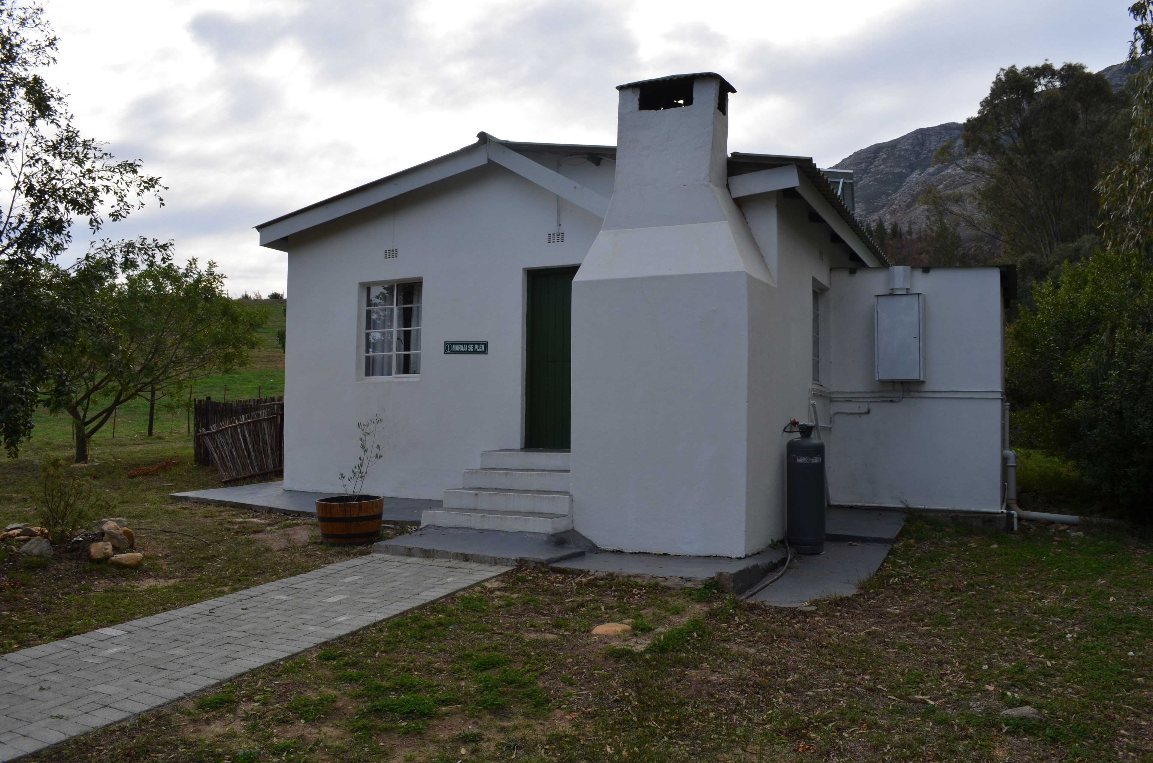 Um edifício branco com porta verde, degraus que levam à entrada e uma chaminé.