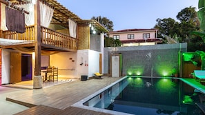 Uma área de piscina com deck de madeira, um espaço de estar pequeno e um espaço ao ar livre coberto com varanda.
