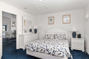 Quarto com cama, duas mesas de cabeceira, cômoda, espelho e duas fotos emolduradas na parede.