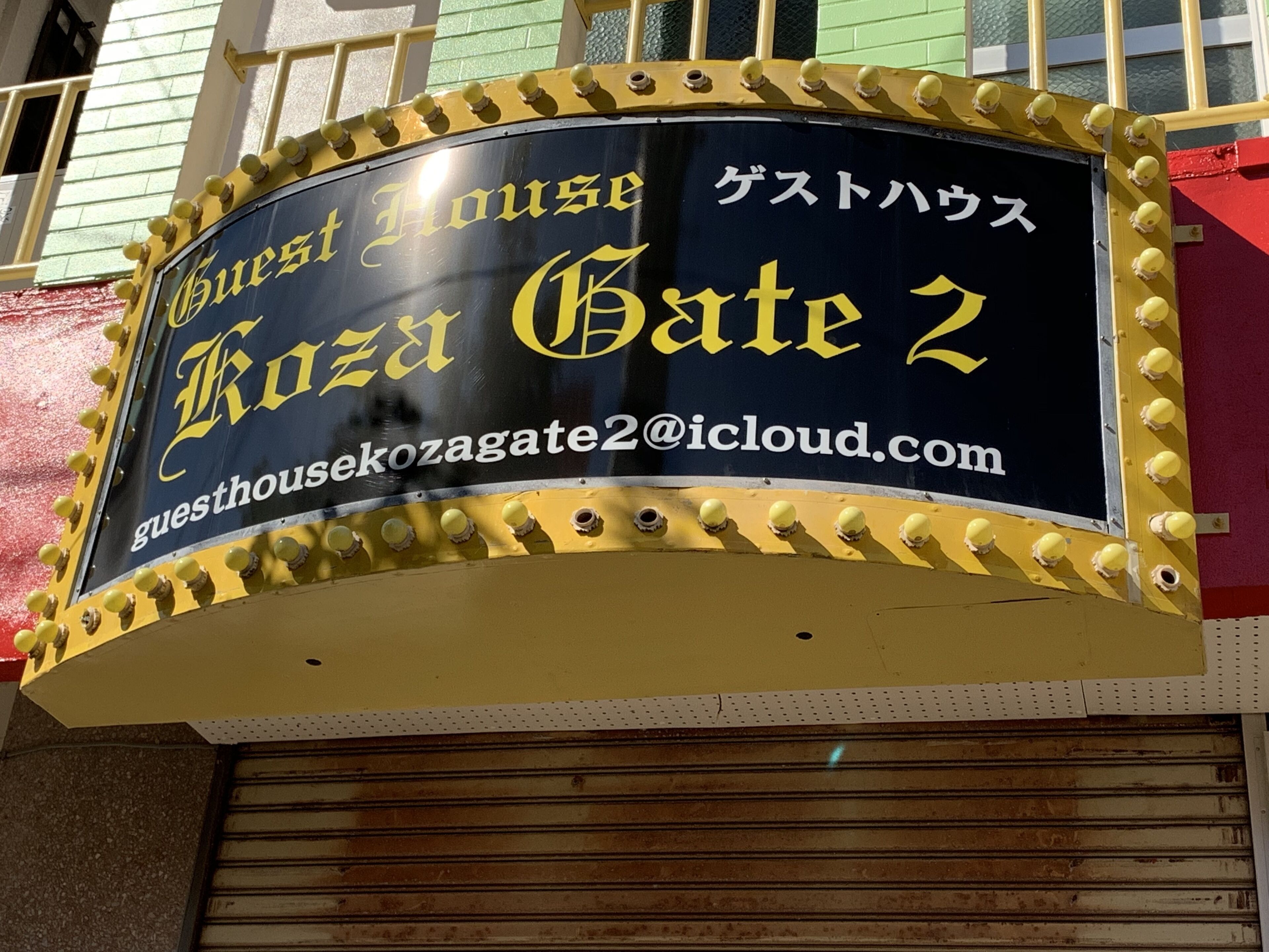 Uma placa curva com o texto 'Guest House Koza Gate 2' e um endereço de e-mail.
