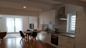 Cozinha moderna com armários brancos, área de refeições com mesa e cadeiras, e uma janela grande que oferece iluminação natural.